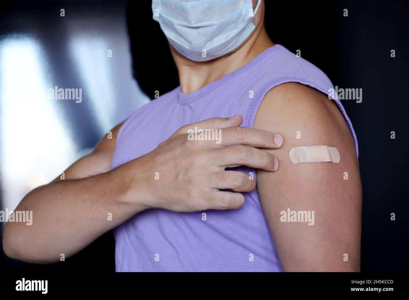 Man in protective face mask showing arm with bandage after receiving ...