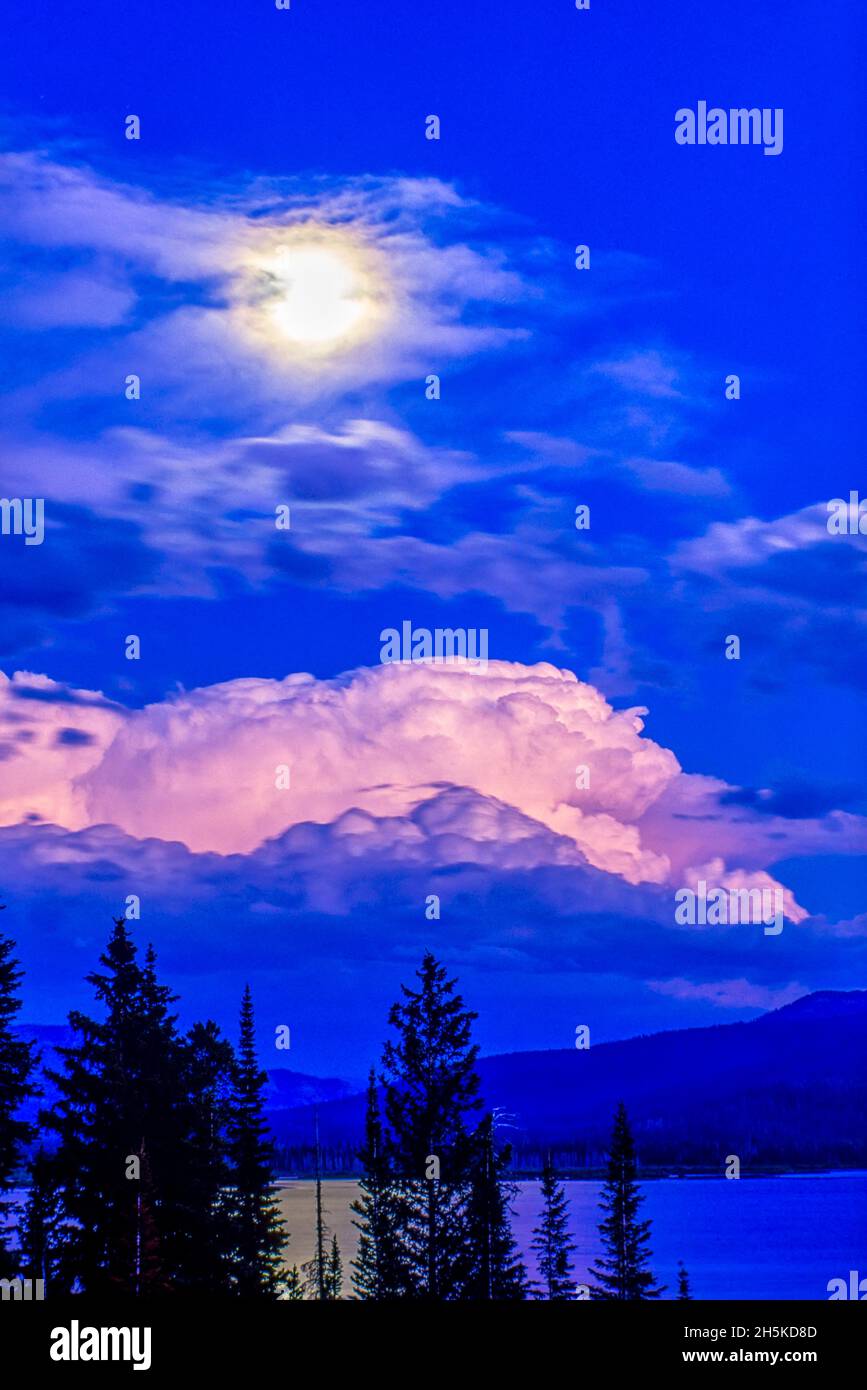 Full Moon in a blue sky lighting up the pink thunder clouds over the ...