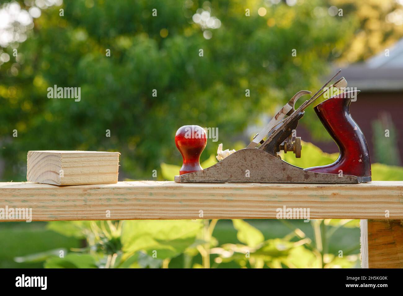 A hand plane tool lays on a wood board in sunlight backyard garden ...