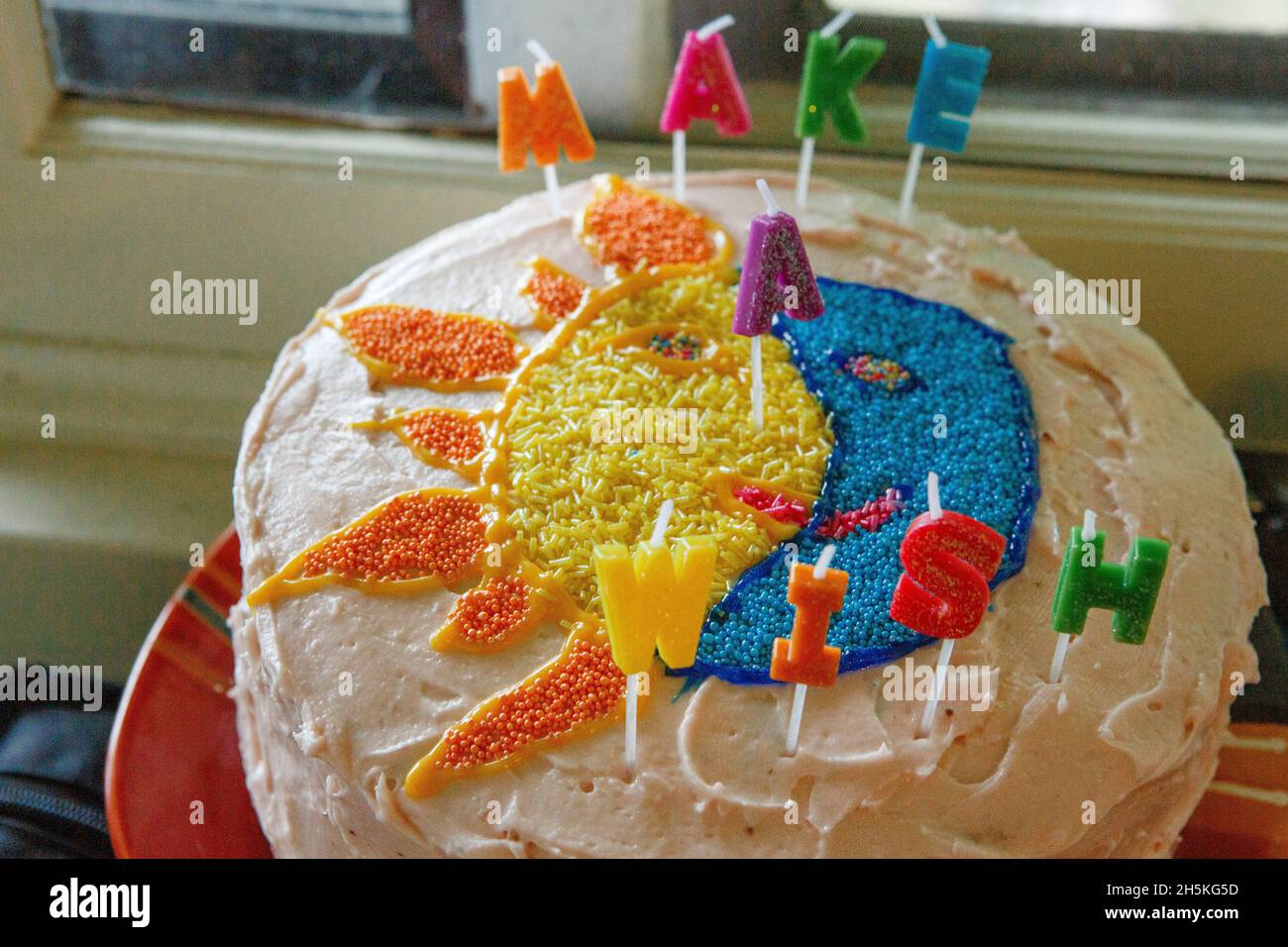 A colorful sun and moon cake with candles that spell "make a wish Stock ...