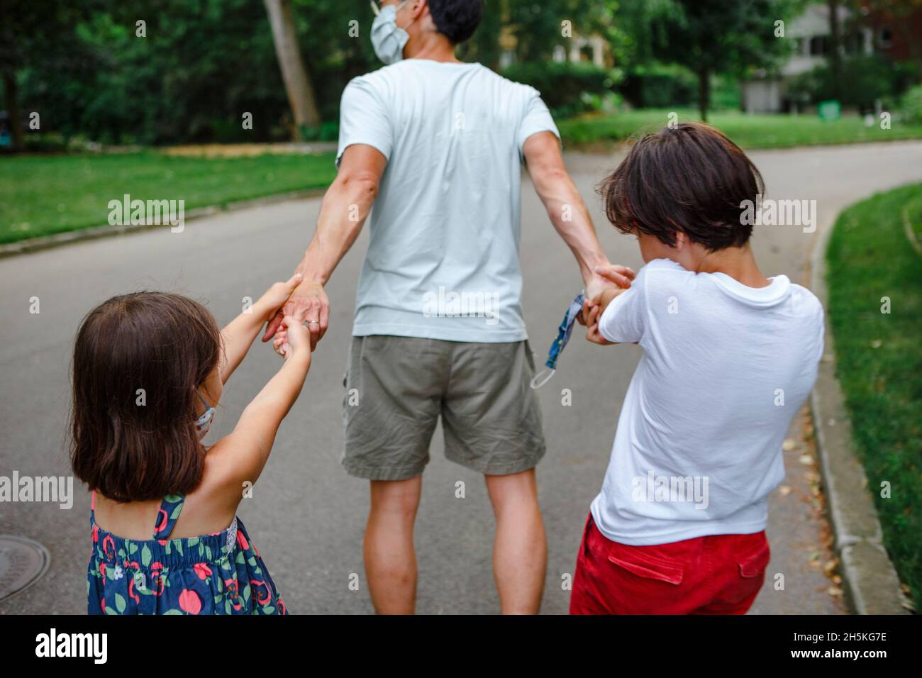 two children pull on fathers hands as they walk down street together ...