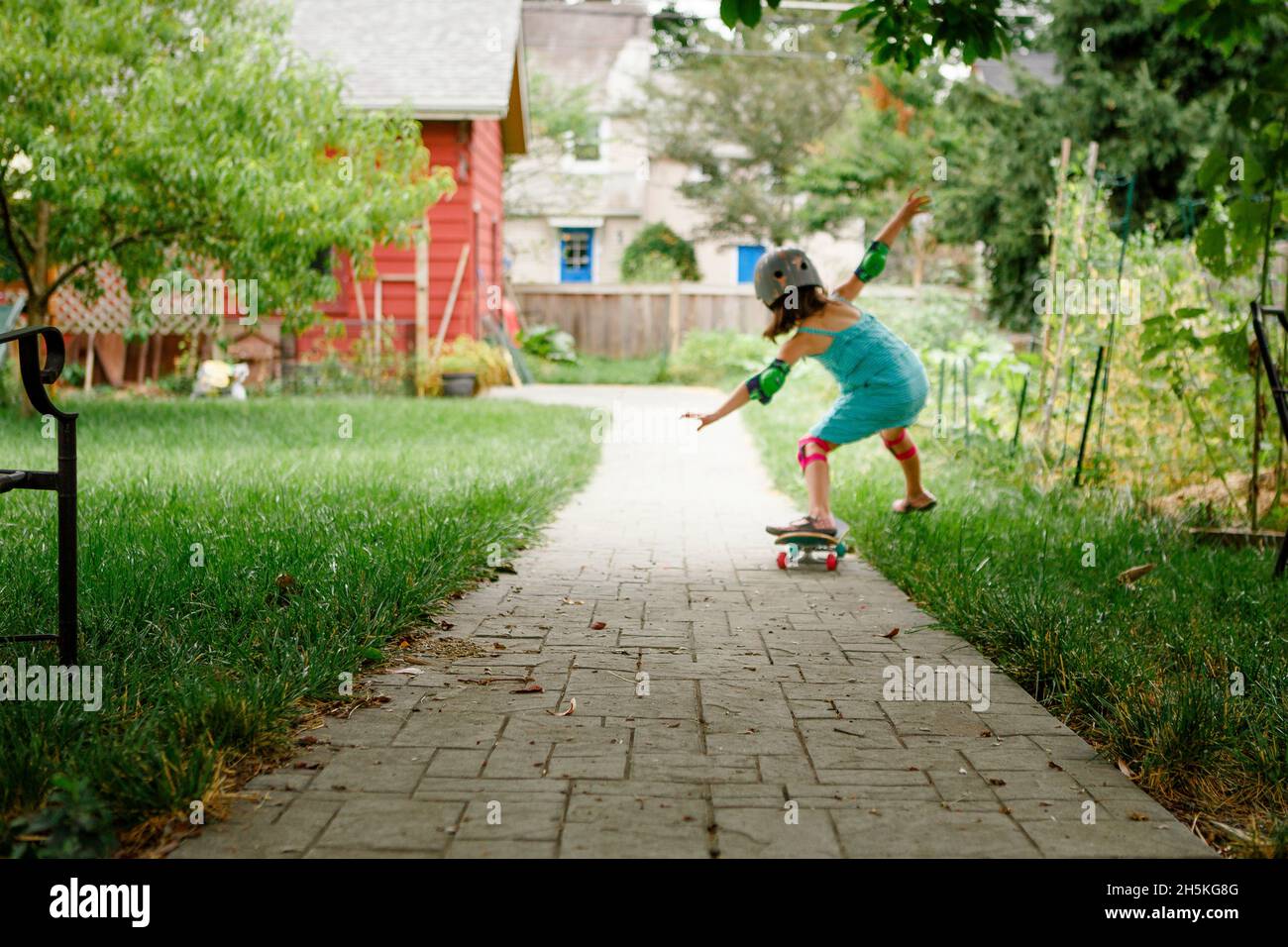 A small child balances one foot on skateboard on backyard path Stock ...