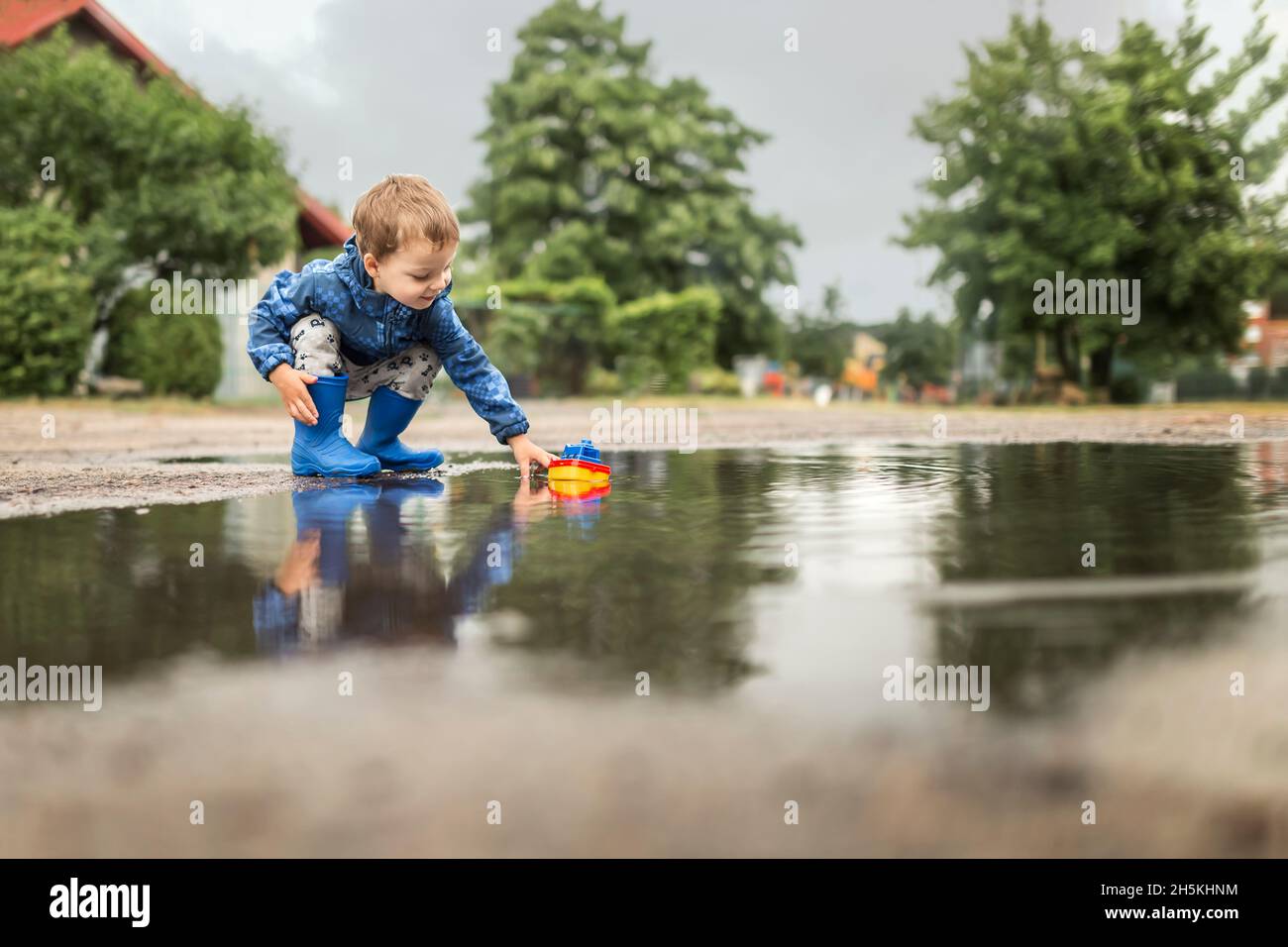 Small blonde boy in blue jacket and blue wellies playing with sh Stock ...