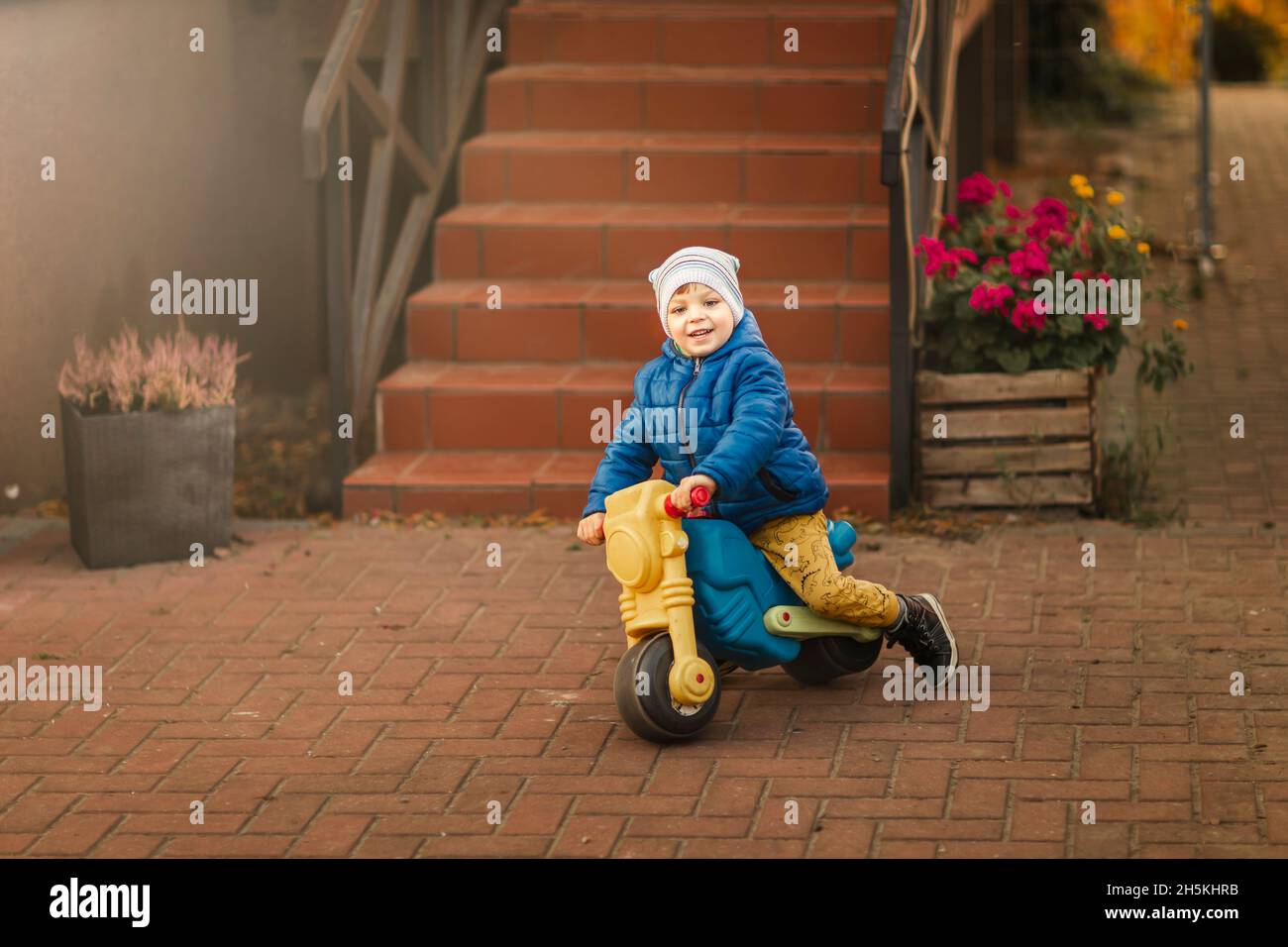 Little boy in blue jacket riding toy motorbike next to staircase Stock ...
