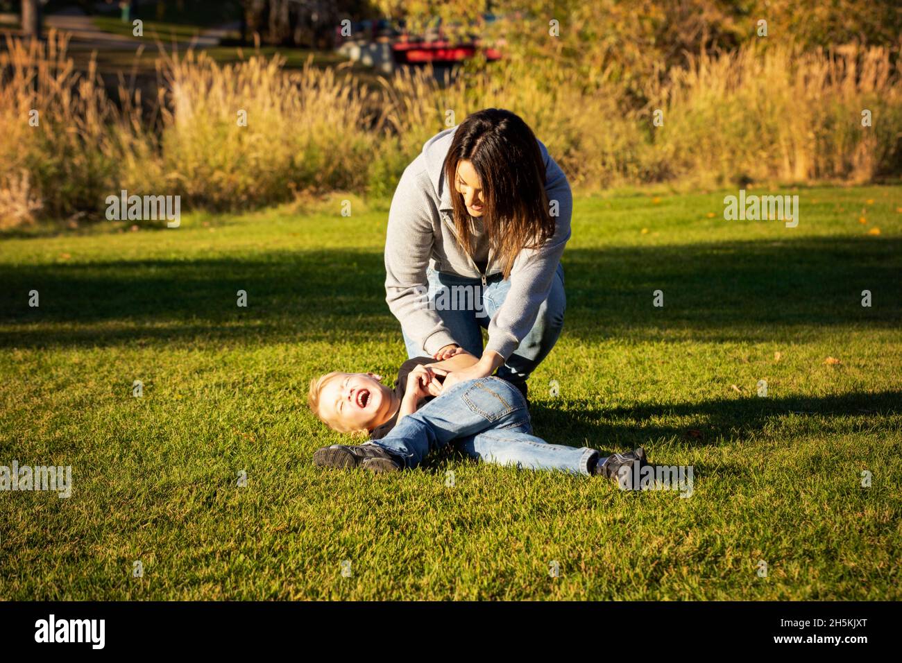 Mother and young son roughhousing on the grass in a city park; St ...