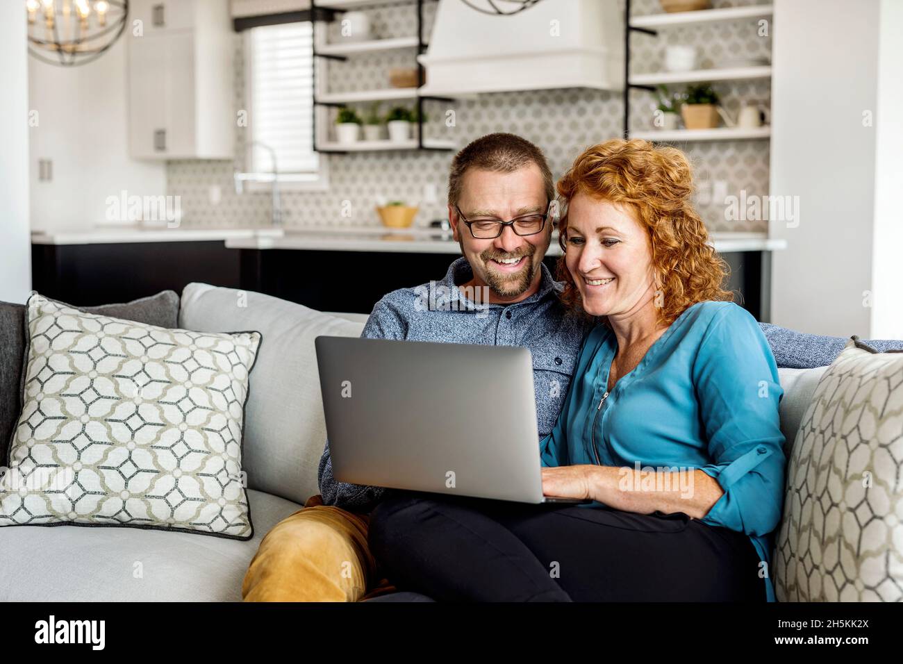 Married couple sitting on a couch at home using their laptop computer ...