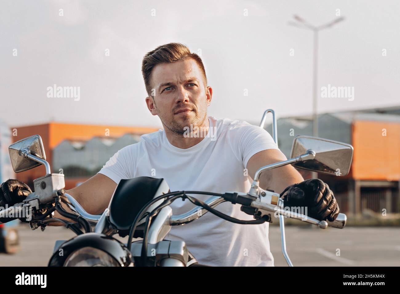 Attractive stylish young man in white T-shirt sits on a motorcycle ...