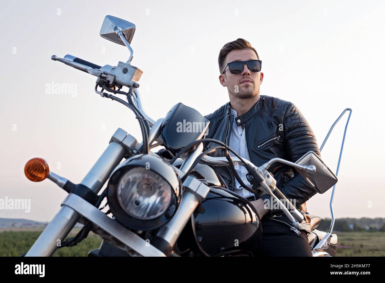 Stylish young attractive guy in sunglasses sits on a motorcycle ...