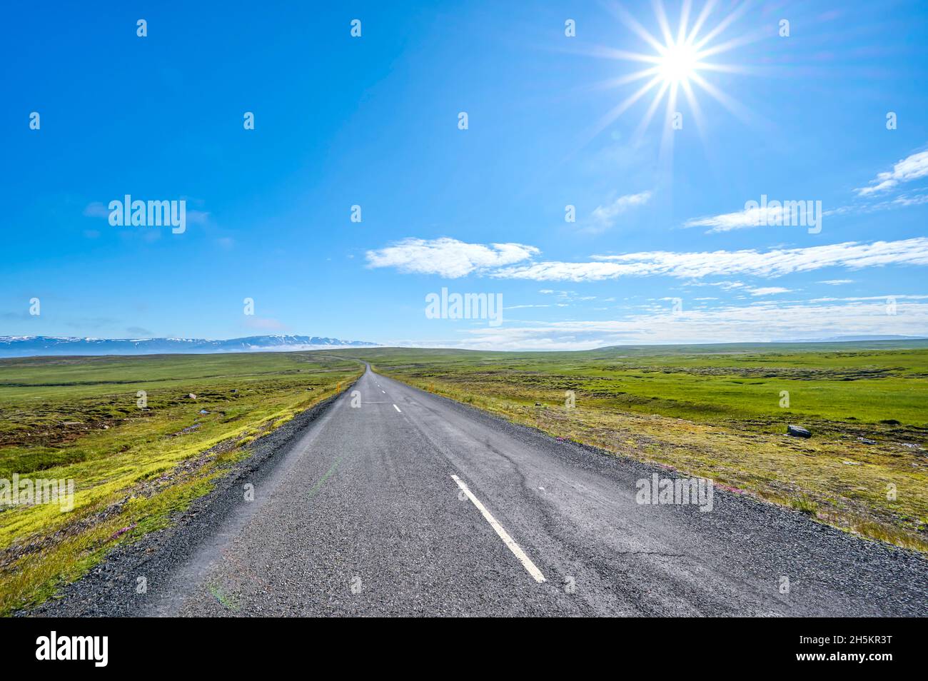 Vast empty road in summer with sunburst in bright blue sky overhead ...