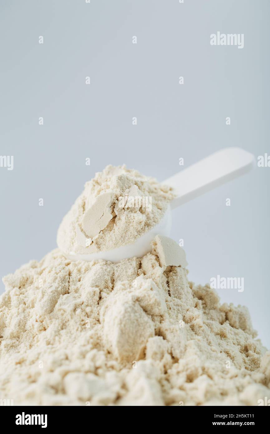 A pile of protein powder with a measuring spoon on a white background ...