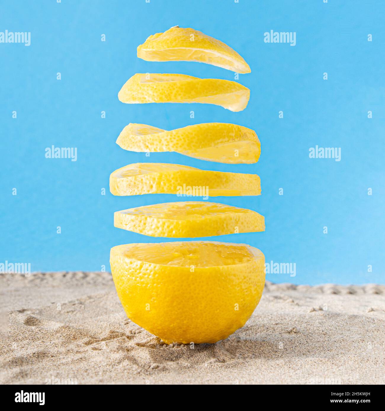 Lemon on beach sand with slices floating in the air on a pastel blue ...