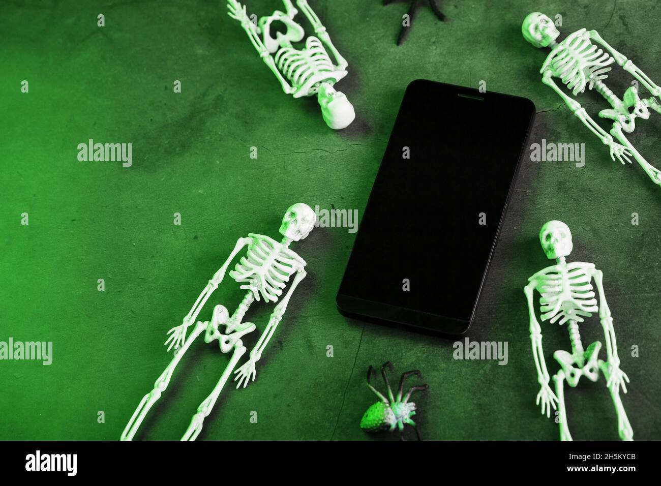 Four skeletons are lying near the smartphone on a dark background ...