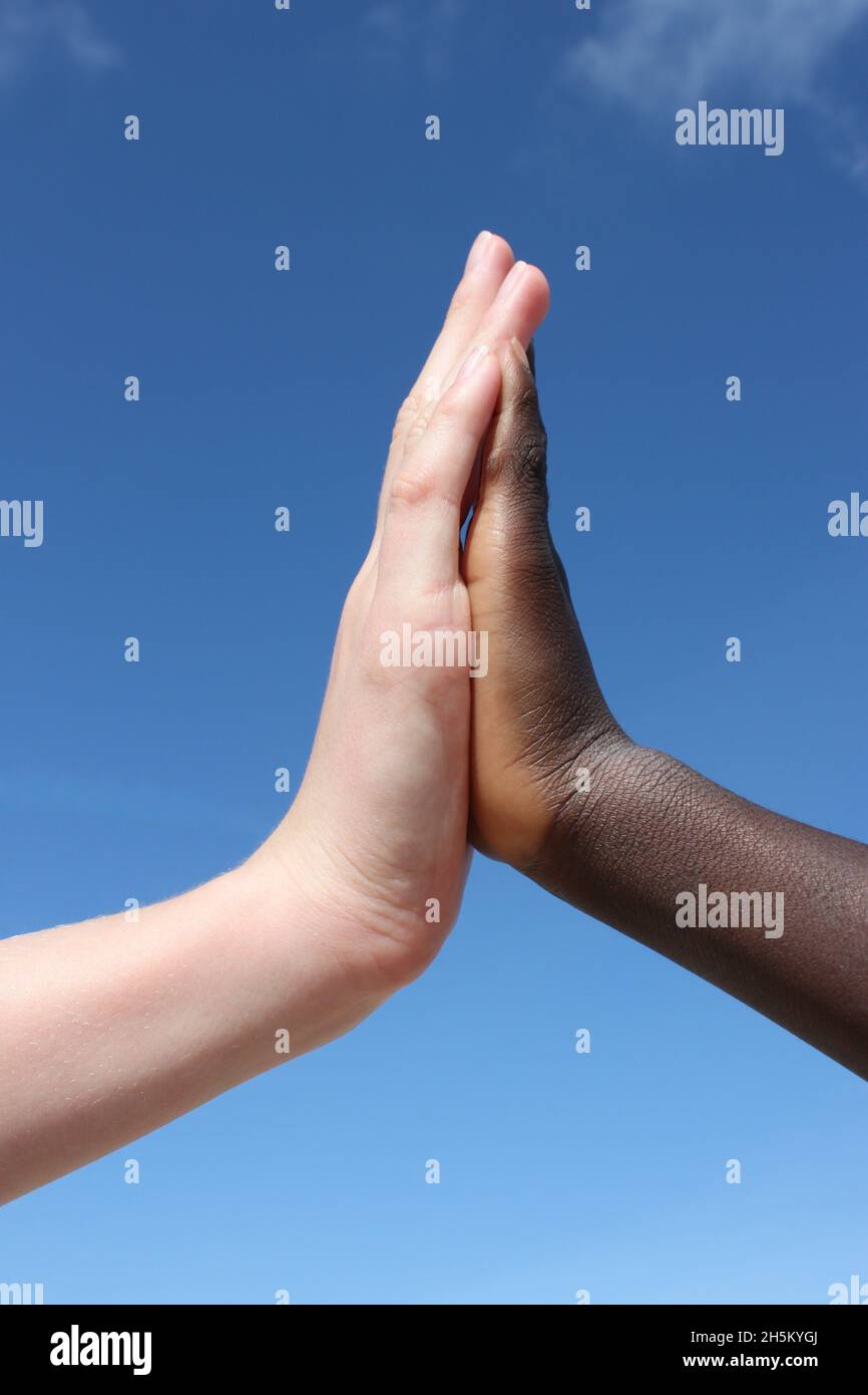 a white-skinned hand and a black-skinned hand high-five each other in ...