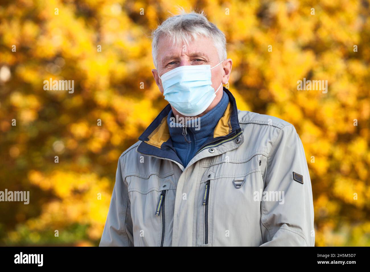 Old man with medical mask wearing on his face, yellow leaves background ...
