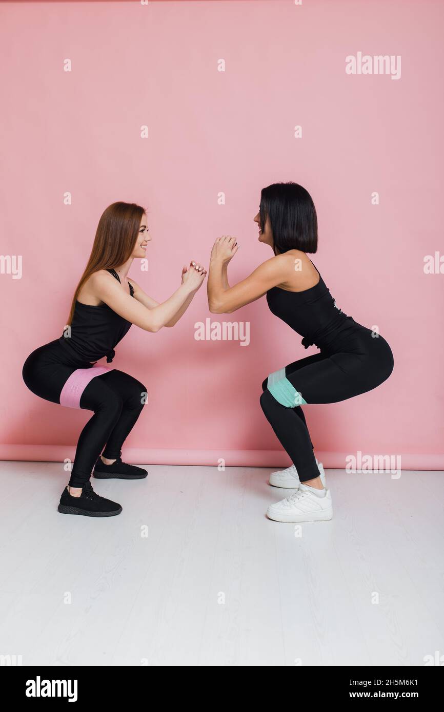 athletic girls in black sportswear on a pink background doing squats ...