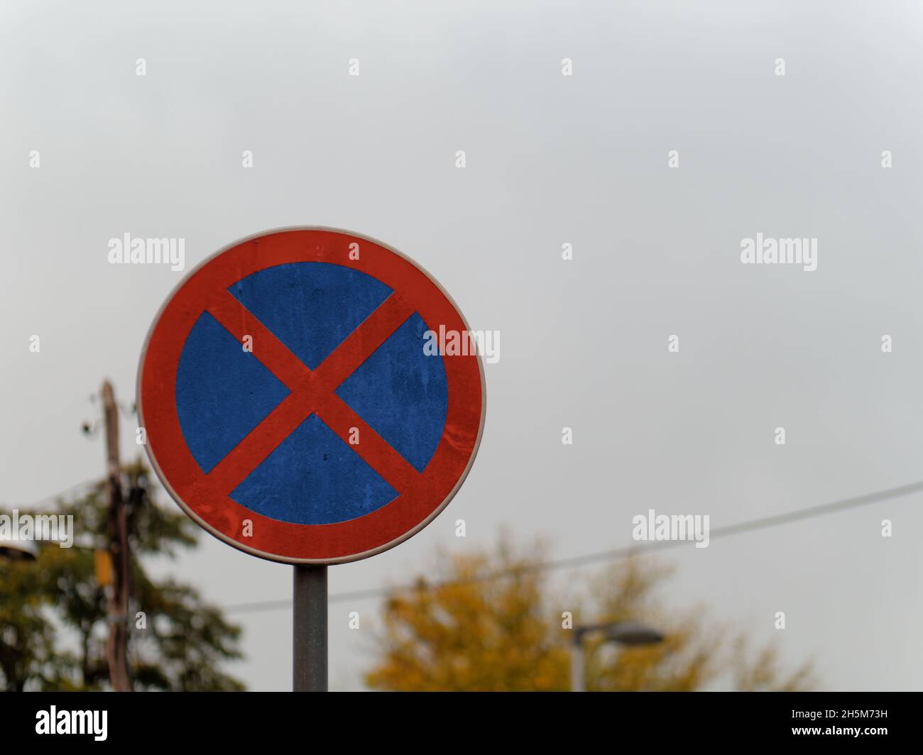 Red and blue No Parking road sign attached on a pole against a gray sky ...