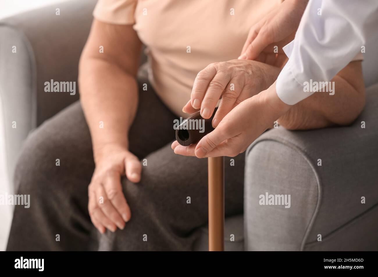 Hands of young woman and her grandmother with walking stick at home ...