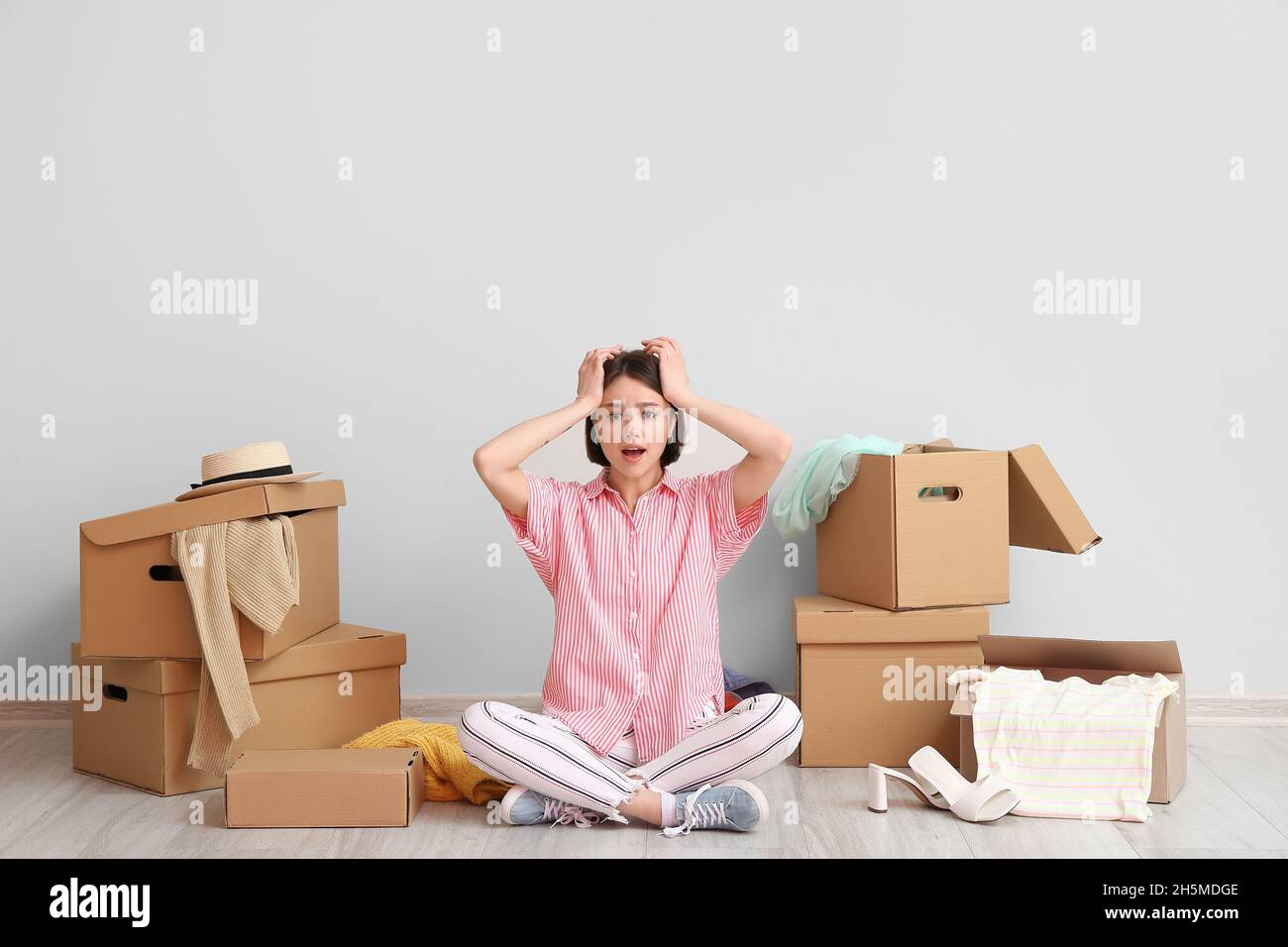Stressed young woman with wardrobe boxes and things near light wall ...