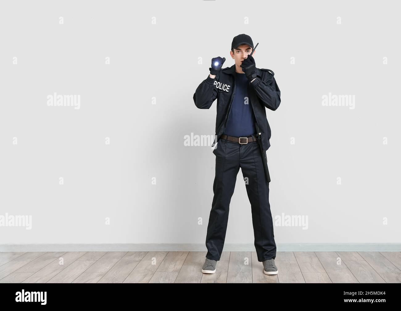 Young policeman with two-way radio and flashlight near light wall Stock ...
