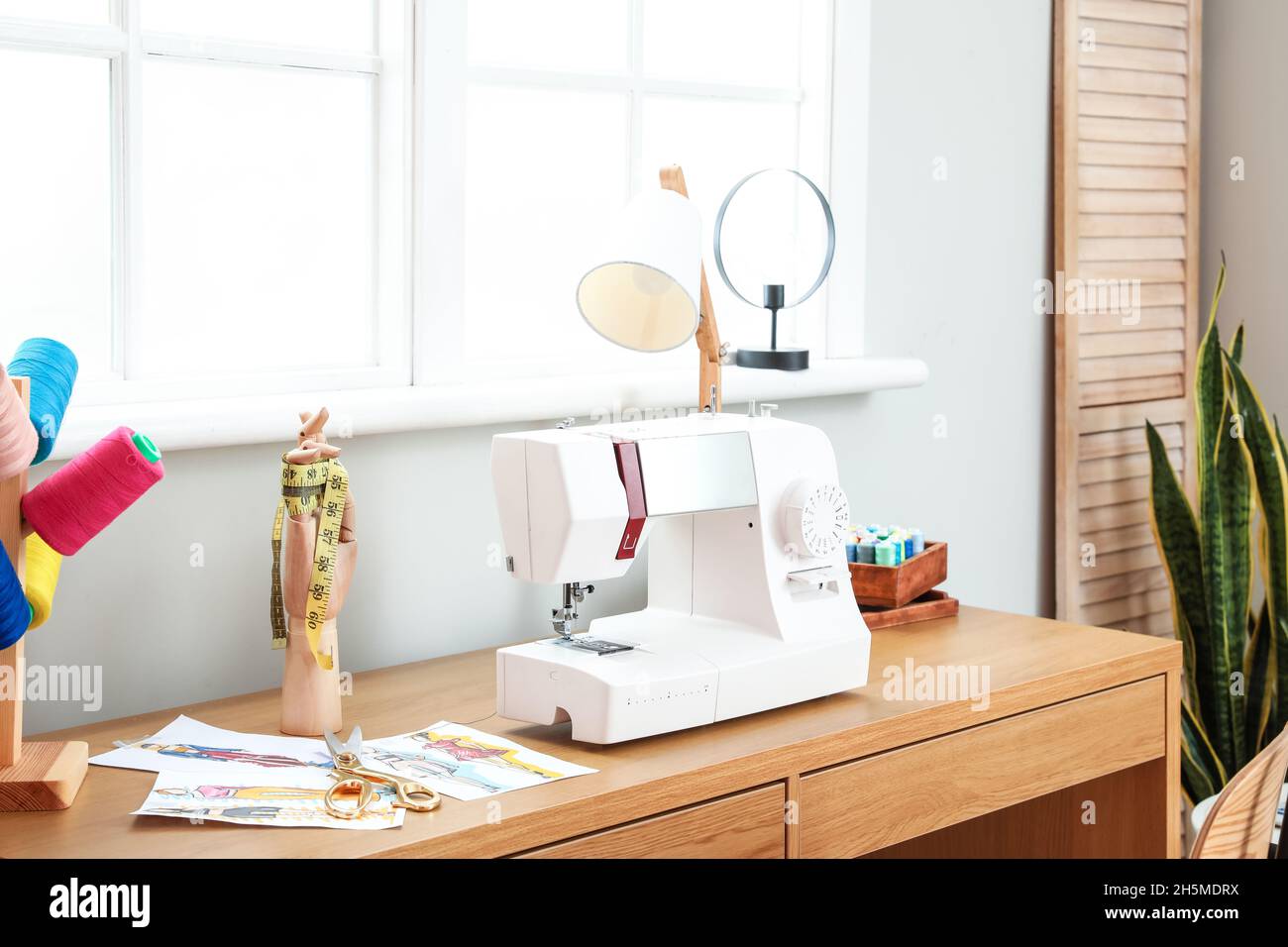 Modern tailor's workplace with sewing machine and sketches near window ...