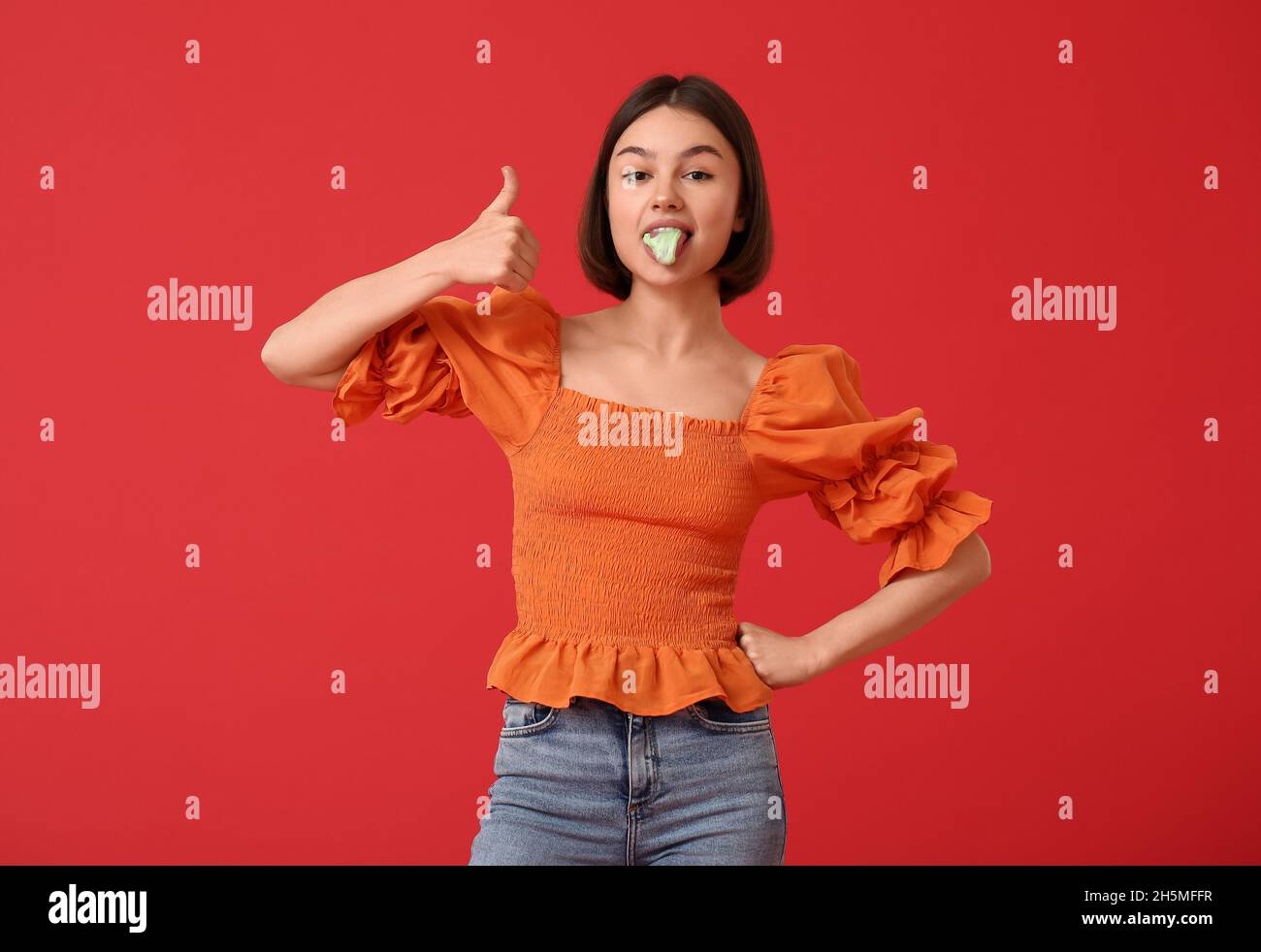 Young woman with chewing gum showing thumb-up on color background Stock ...