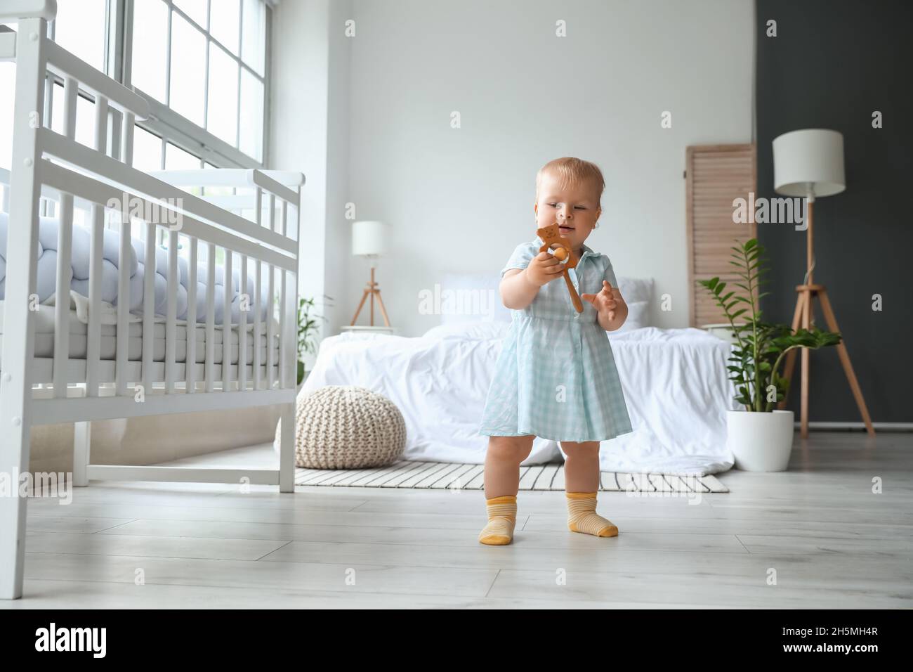 Cute baby girl with rattle learning to walk in bedroom Stock Photo - Alamy