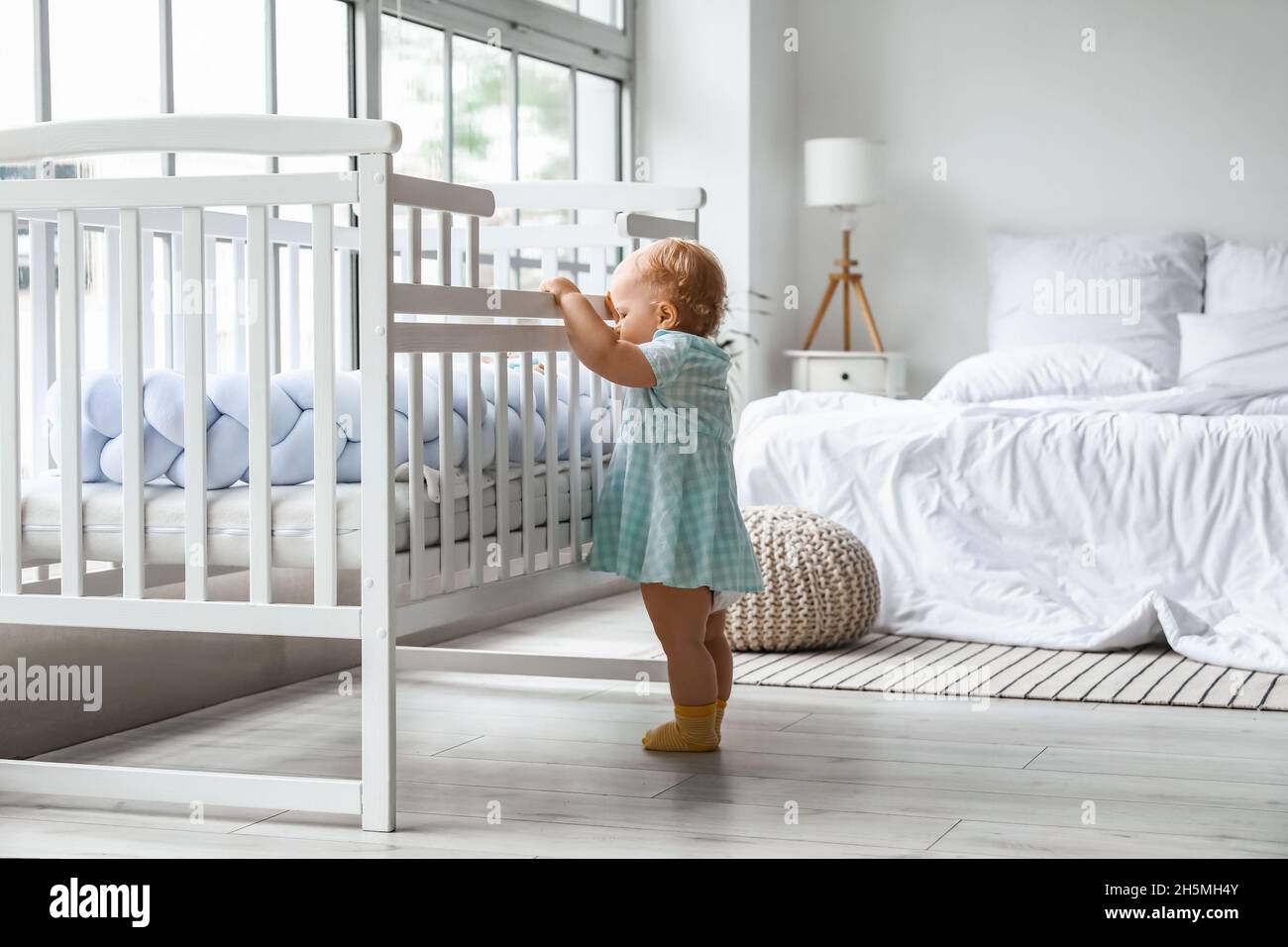 Cute baby girl learning to walk near crib in bedroom Stock Photo - Alamy