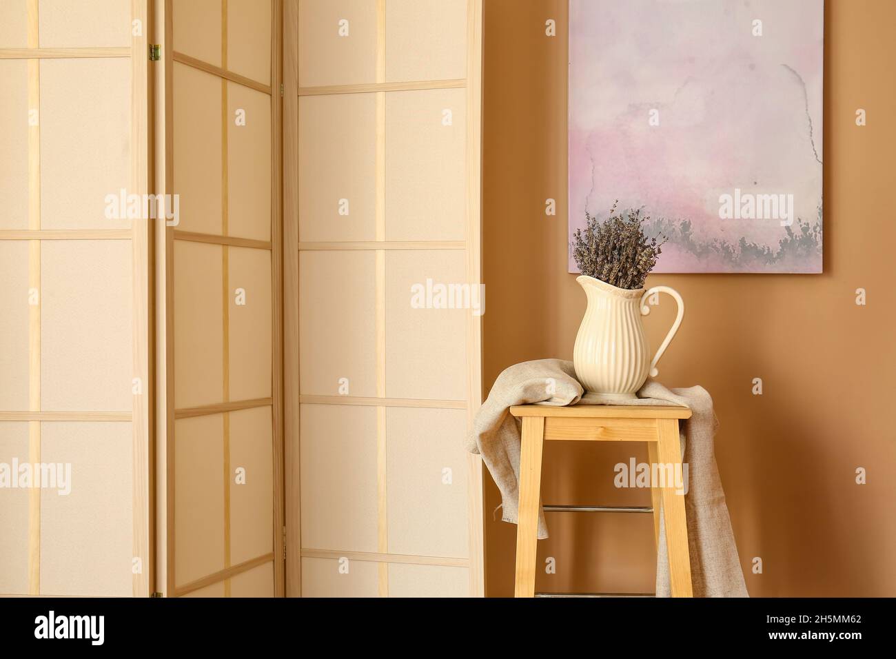 Vase with lavender flowers on stool and folding screen near beige wall ...