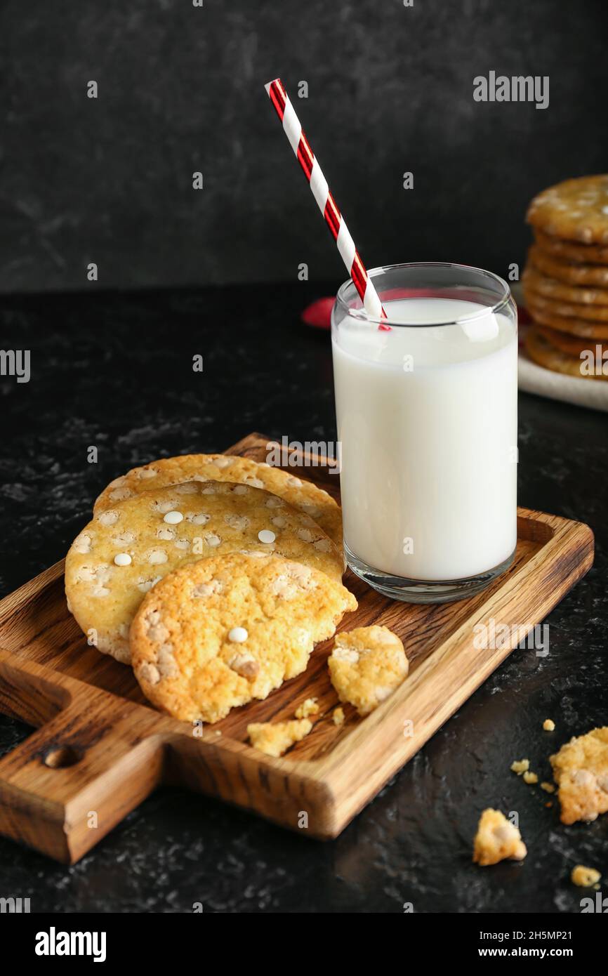 Board with tasty chocolate cookies and glass of milk on dark table ...