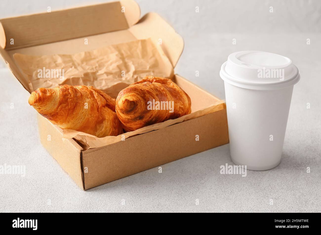 Box with delicious croissants and cup of beverage on white background ...