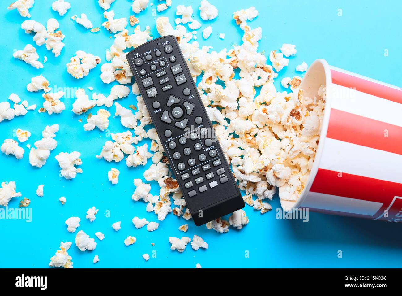Modern TV remote control and bucket with popcorn on color background ...