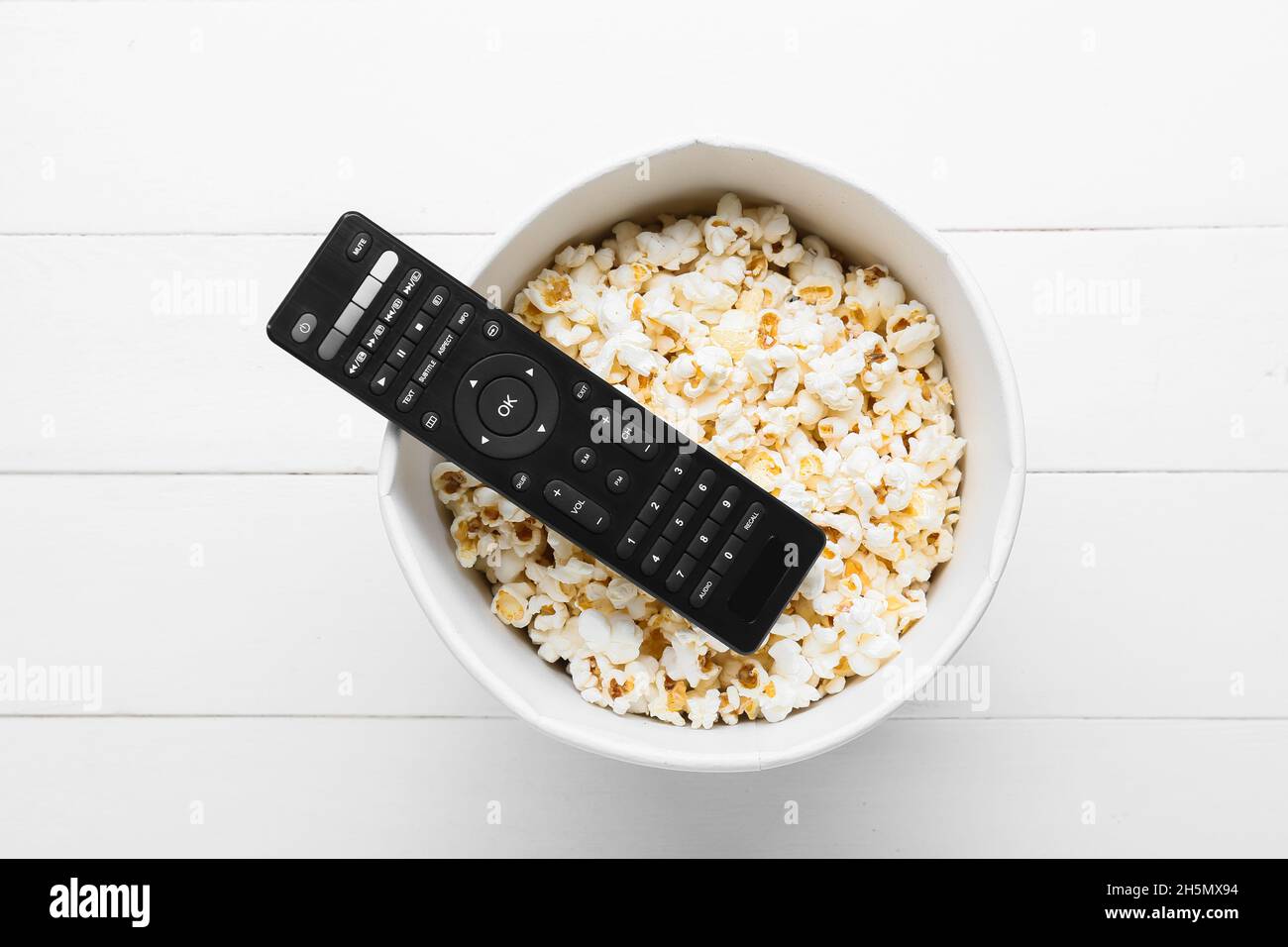 Modern TV remote control and bucket with popcorn on light wooden ...