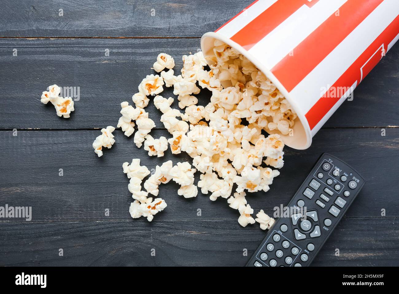 Modern TV remote control and bucket with popcorn on dark wooden ...