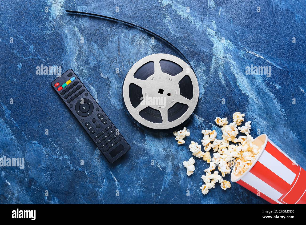 Modern TV remote control, film reel and bucket with popcorn on color ...