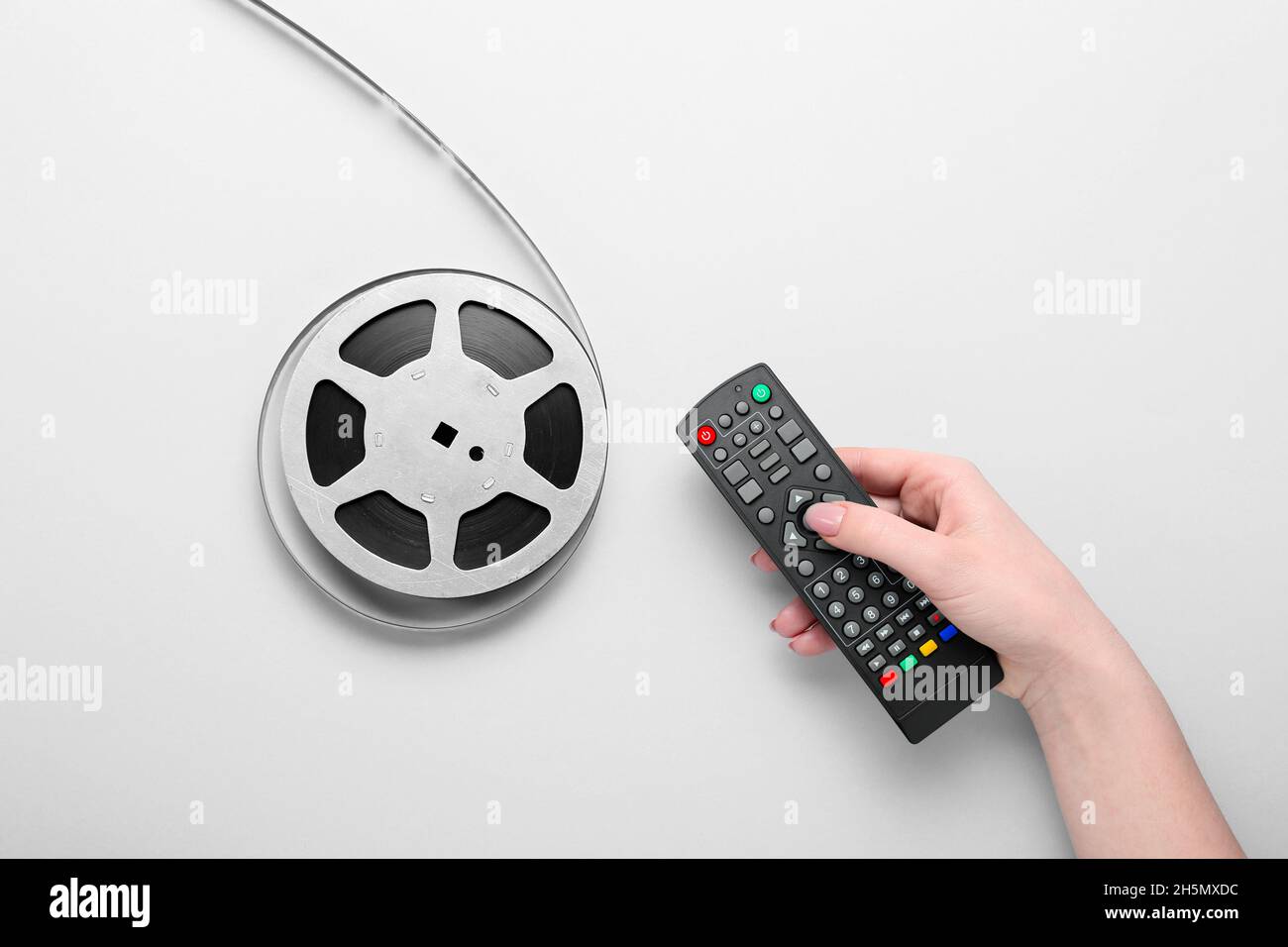 Female hand with TV remote controller and film reel on grey background ...