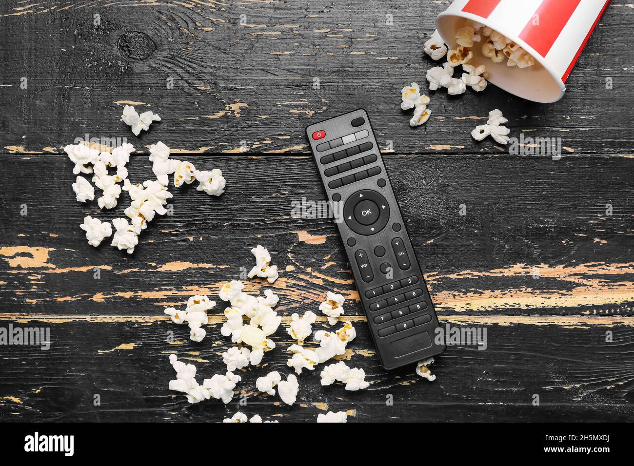 Modern TV remote control and bucket with popcorn on dark wooden ...
