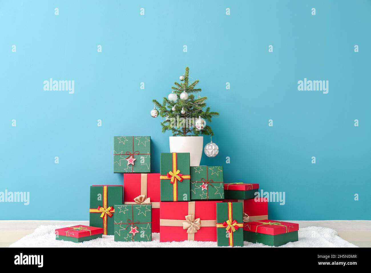 Small Christmas tree with balls and gift boxes near blue wall Stock ...