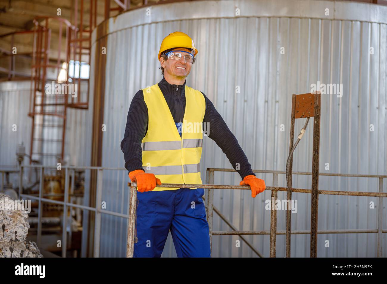 Cheerful man engineer standing near meta storage container at factory ...