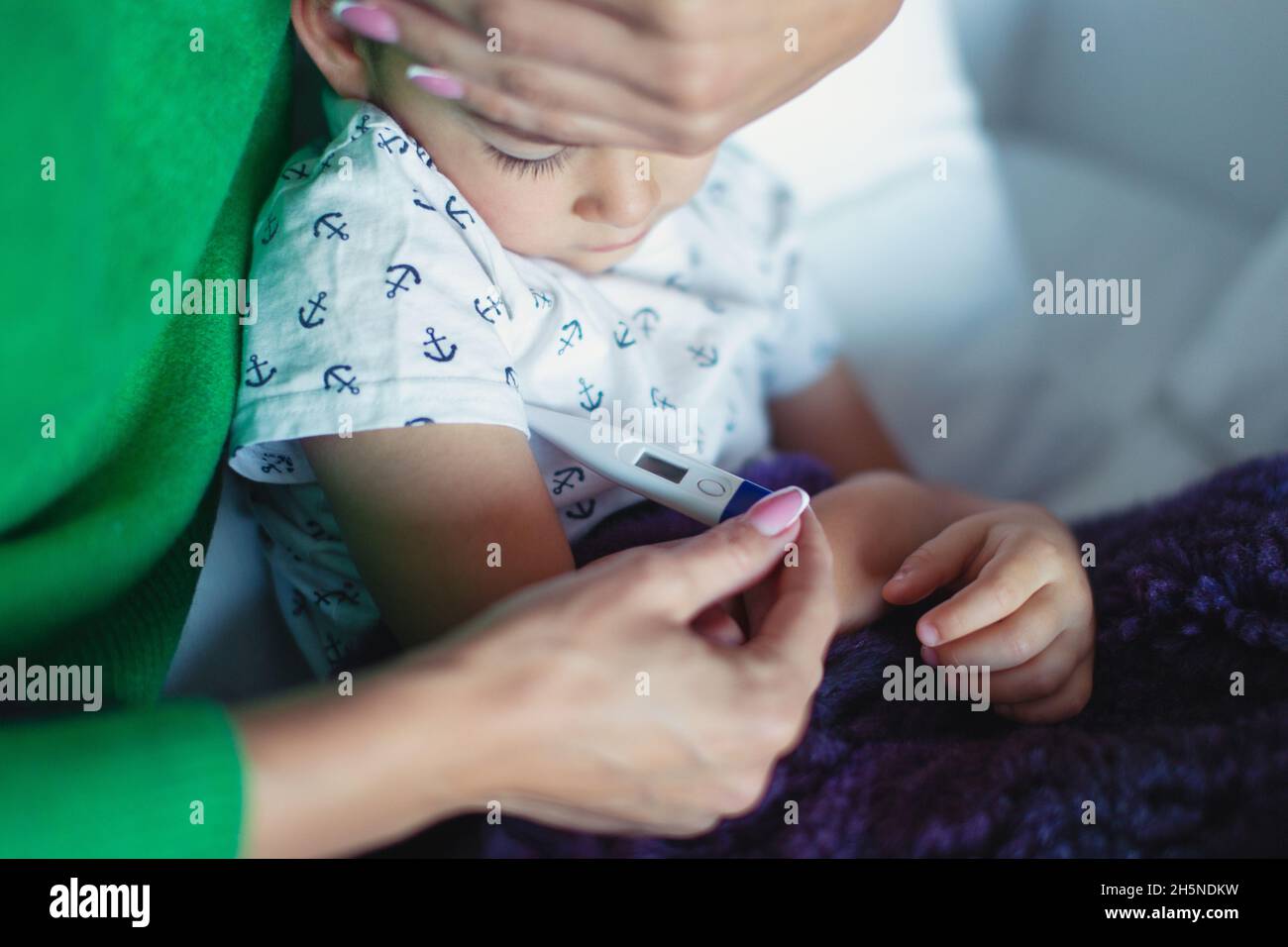 Mother taking temperature to son at home closeup, holding forehead ...