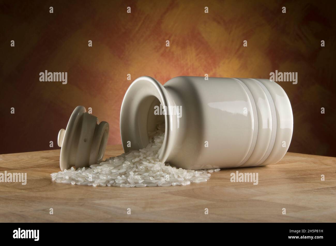 Ceramic canister lying on its side on wood bench with rice spilling out ...