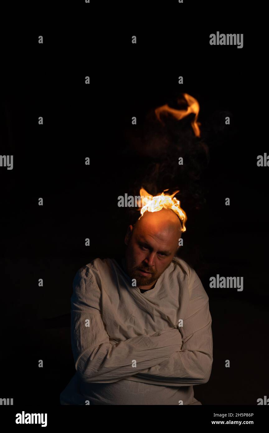 Bald man in a straitjacket with a burning head on a dark background ...