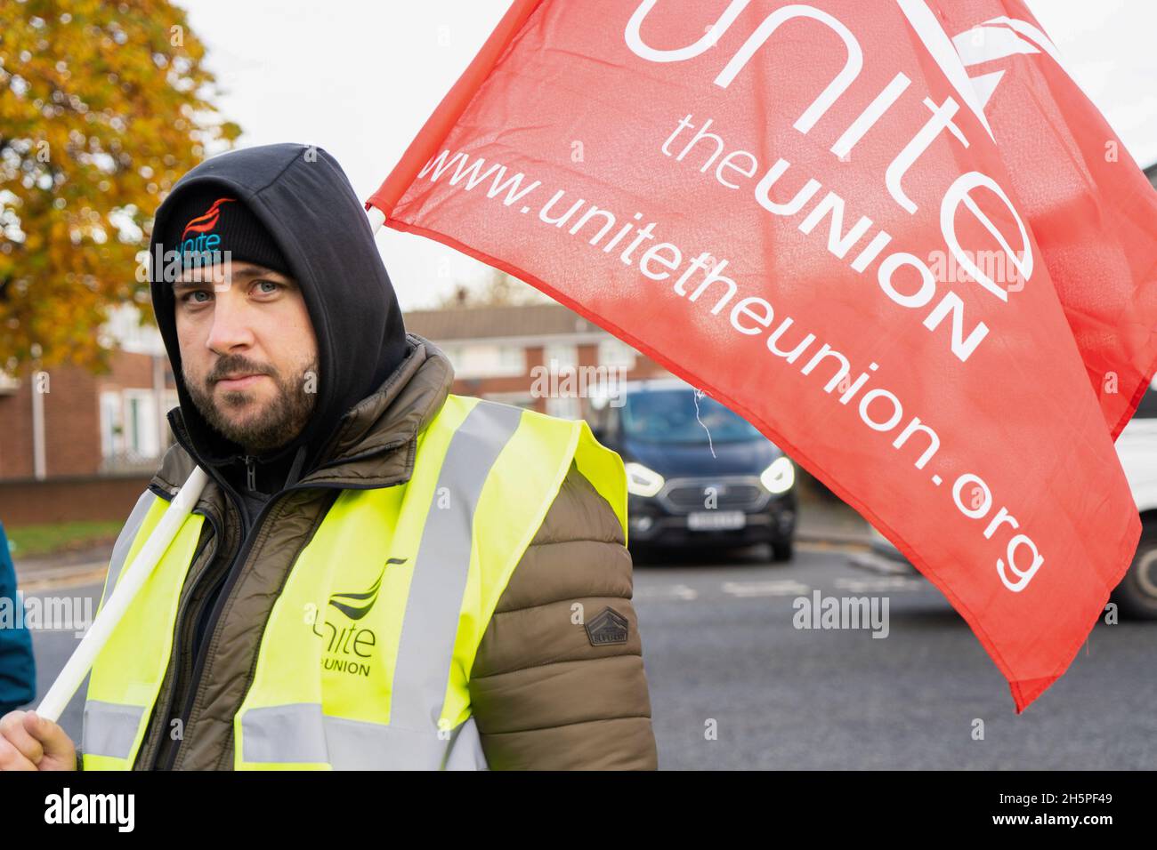 A male bus driver stands on a picket line with a trade union flag ...