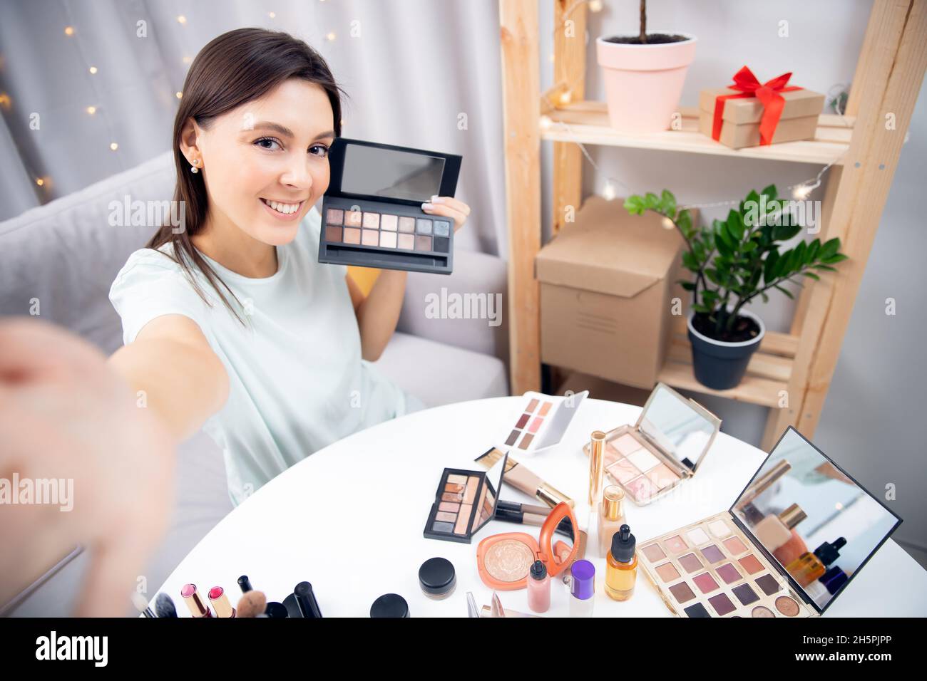 Happy woman vlogger is showing cosmetics products while recording video ...