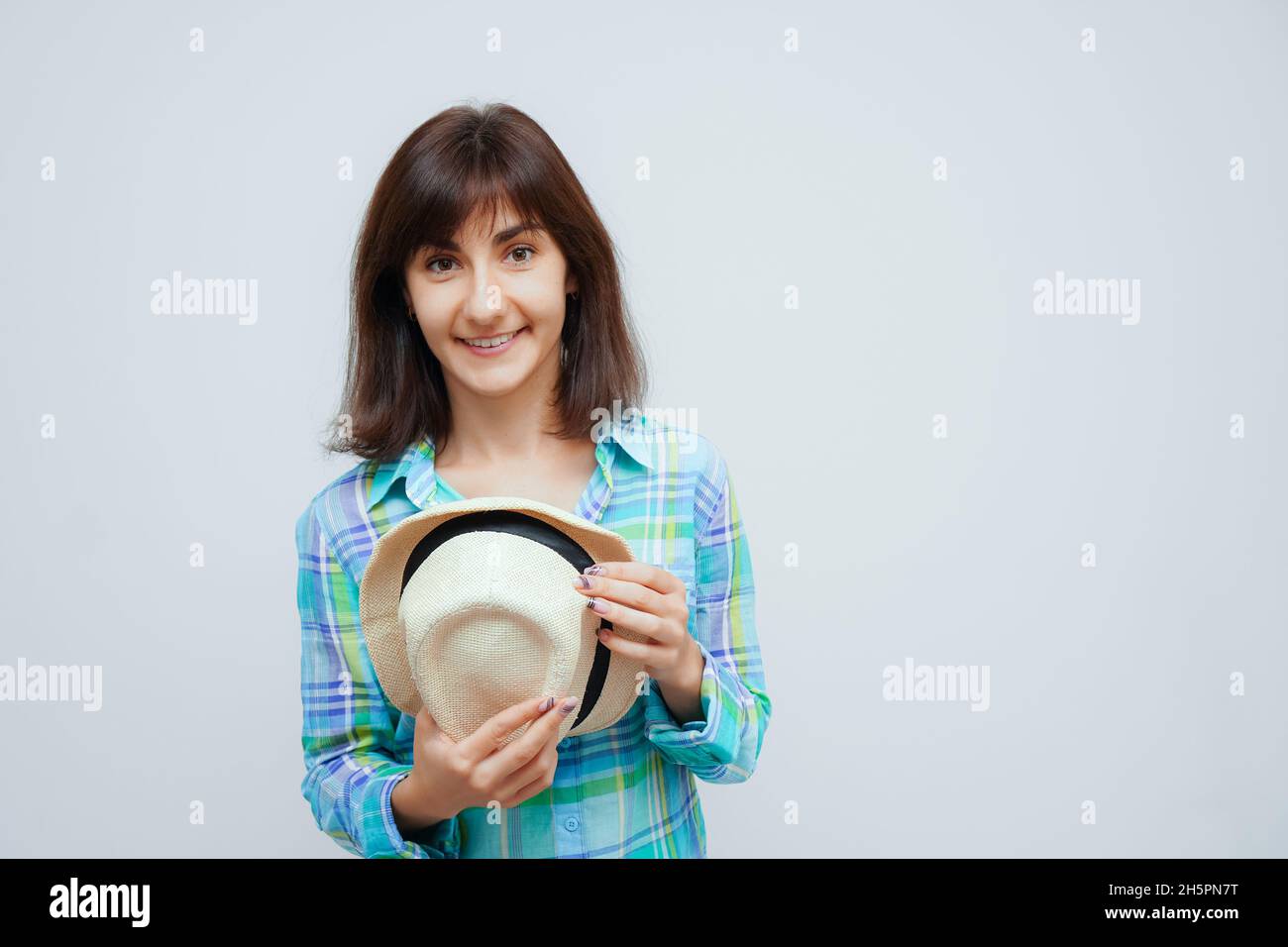 Young smiling brunet caucasian woman taking off hat isolated on gray ...