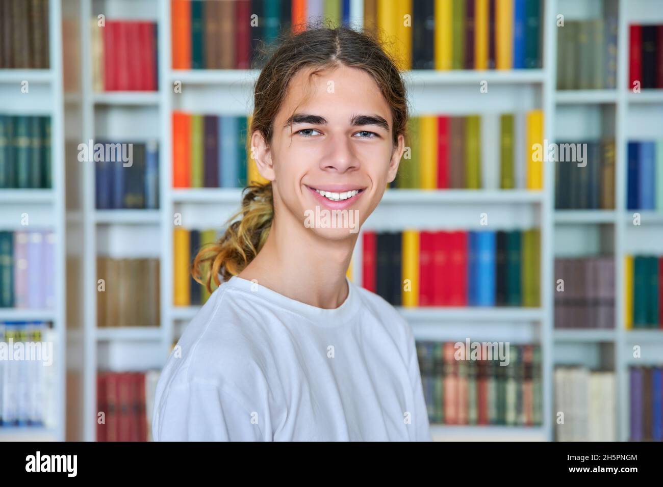 Portrait of a smiling teenage boy looking at the camera in the library ...