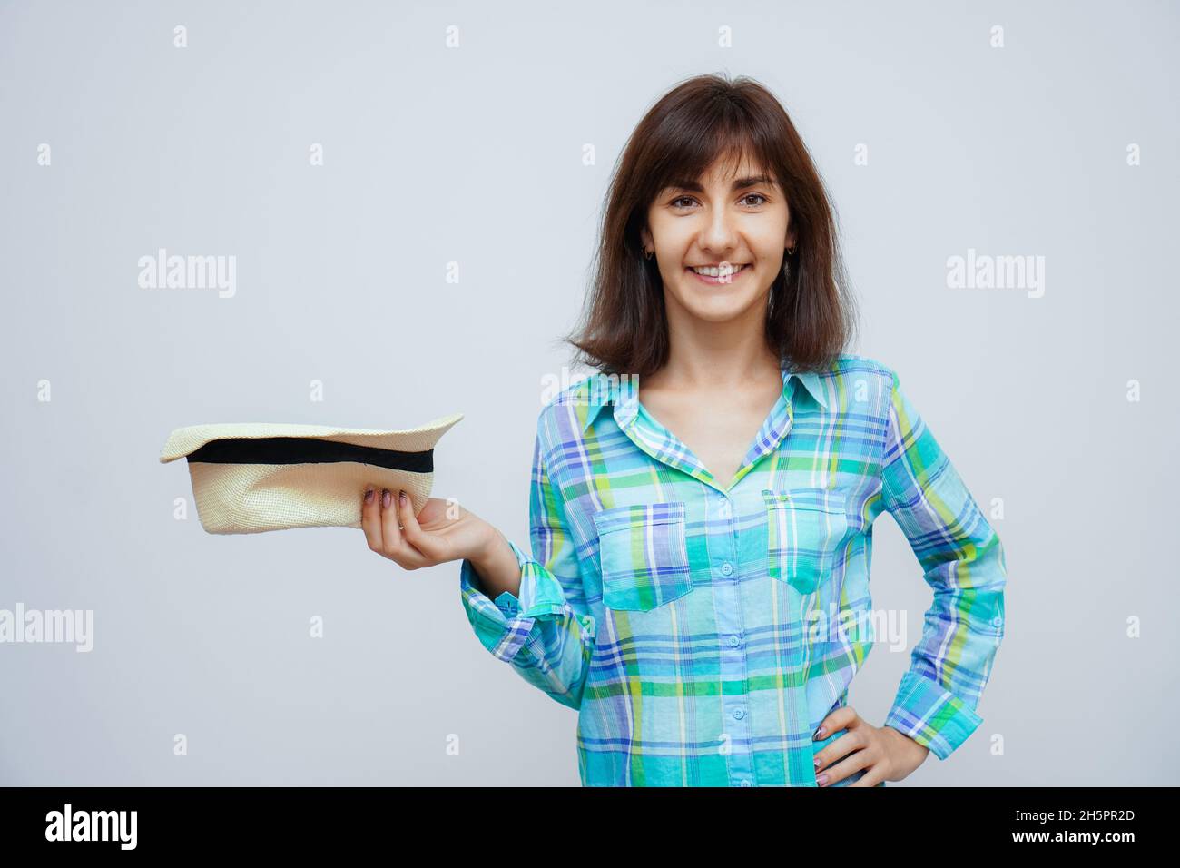 Young smiling brunet caucasian woman taking off hat isolated on gray ...