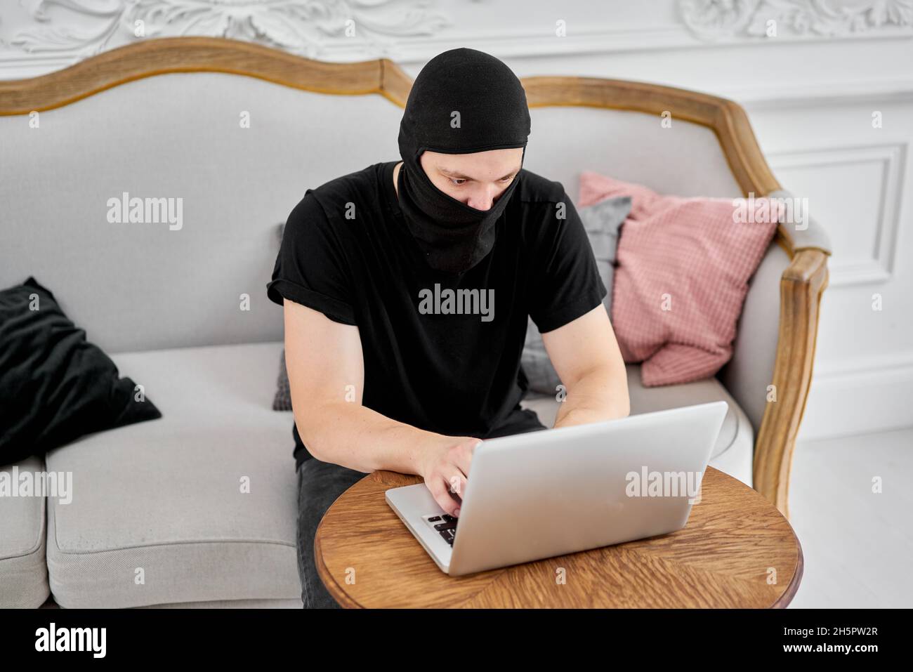 portrait of unrecognizable young hacker in black mask using laptop ...