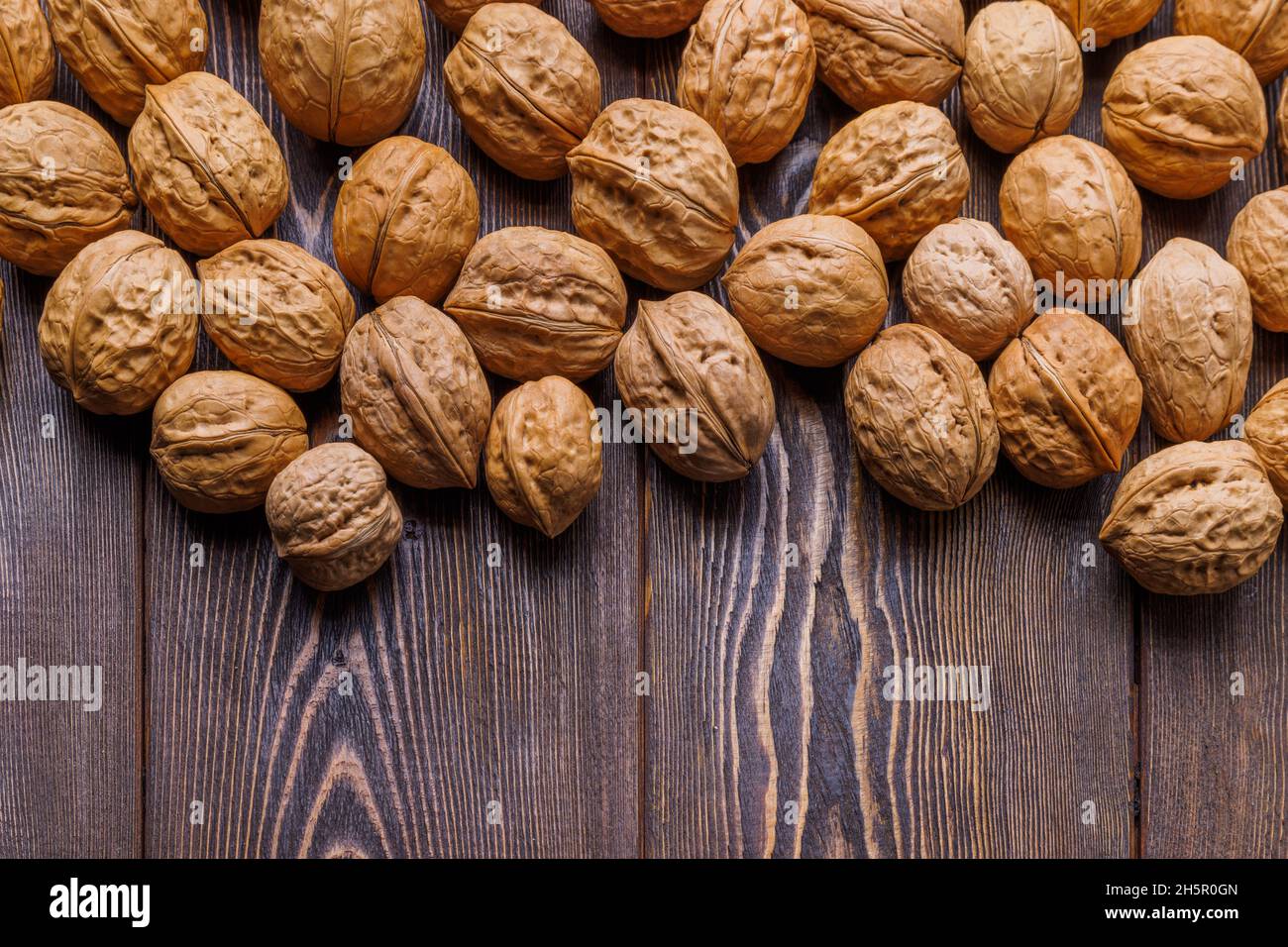 many walnuts with shells randomly scattered on brown wooden surface ...