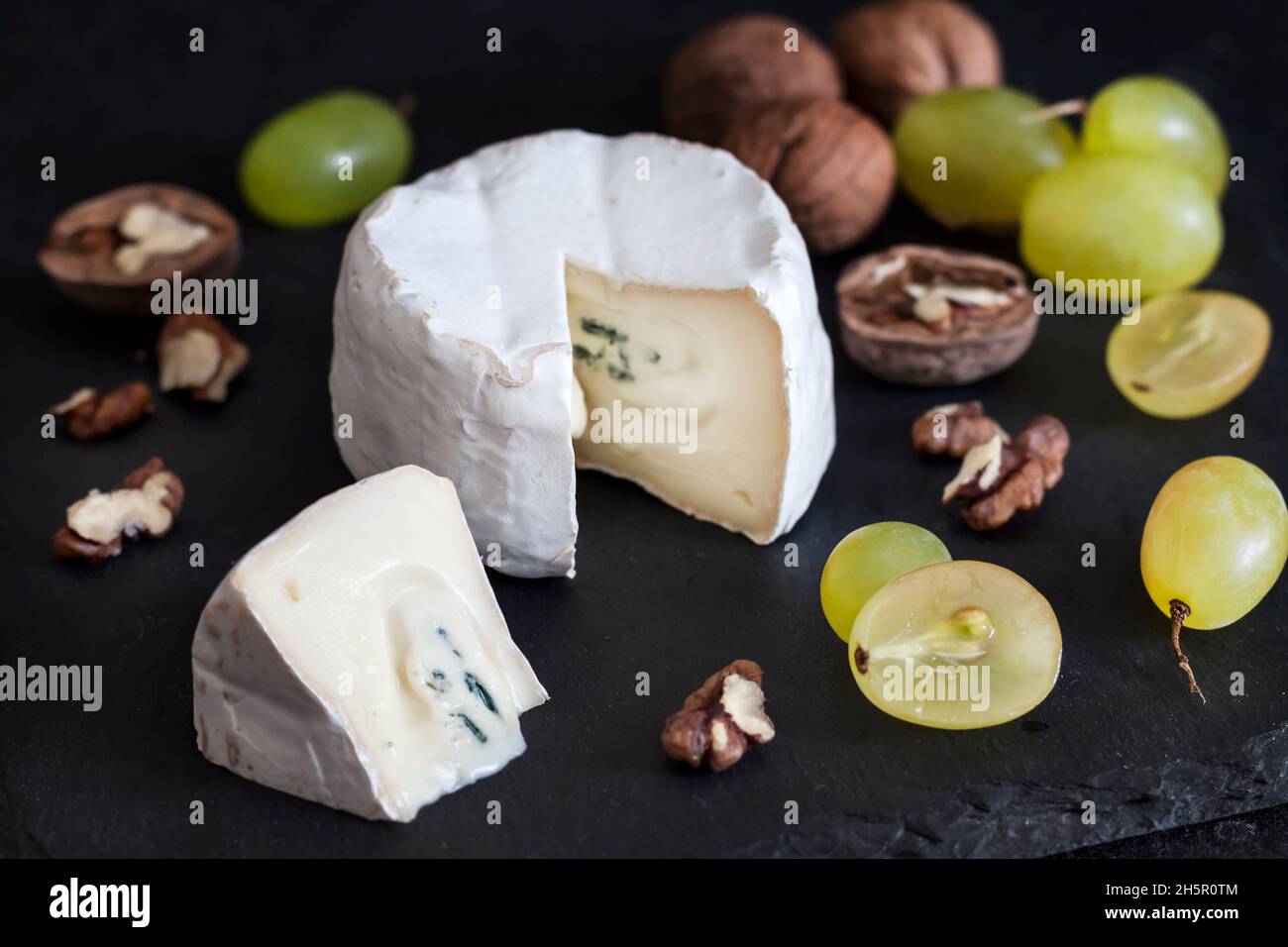Brie type of cheese. Soft cheese with grapes and walnuts on black ...
