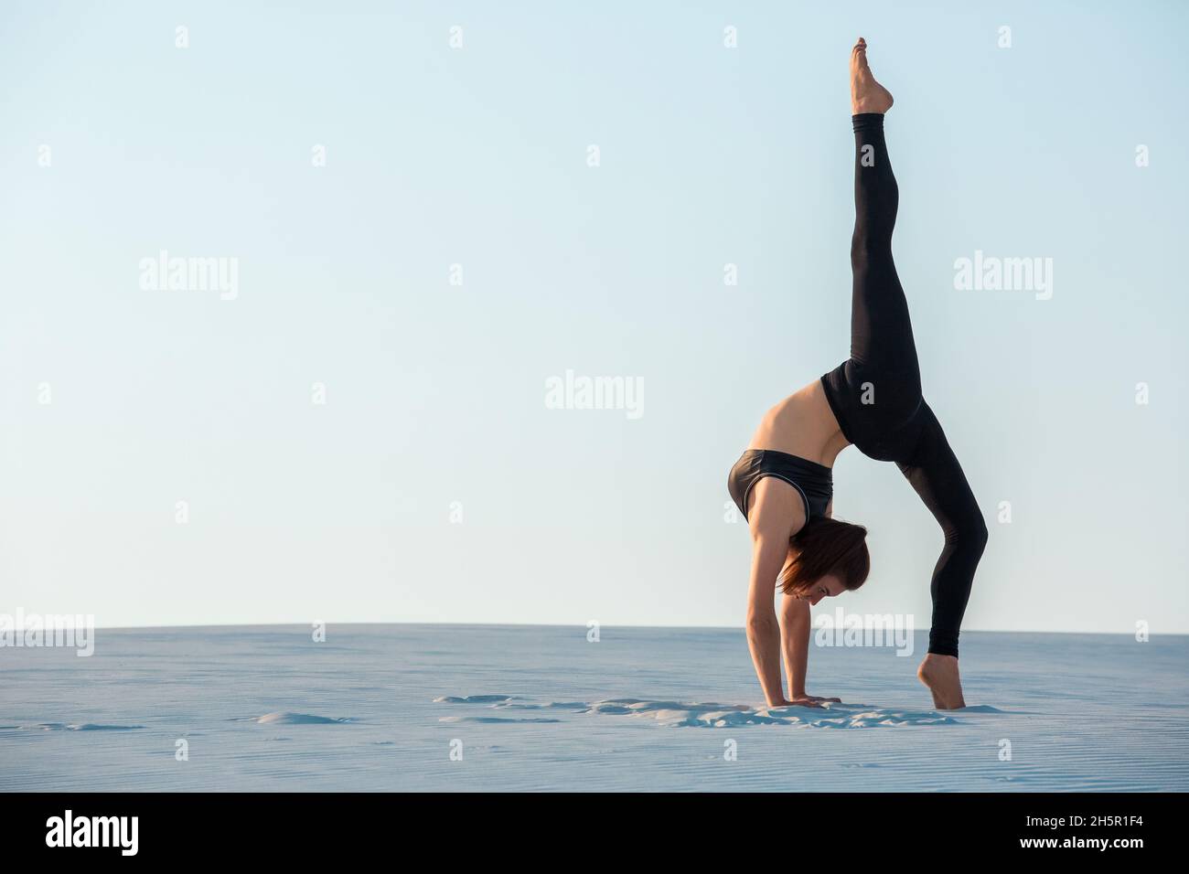 Young woman practicing inversion balancing yoga pose handstand on sand ...